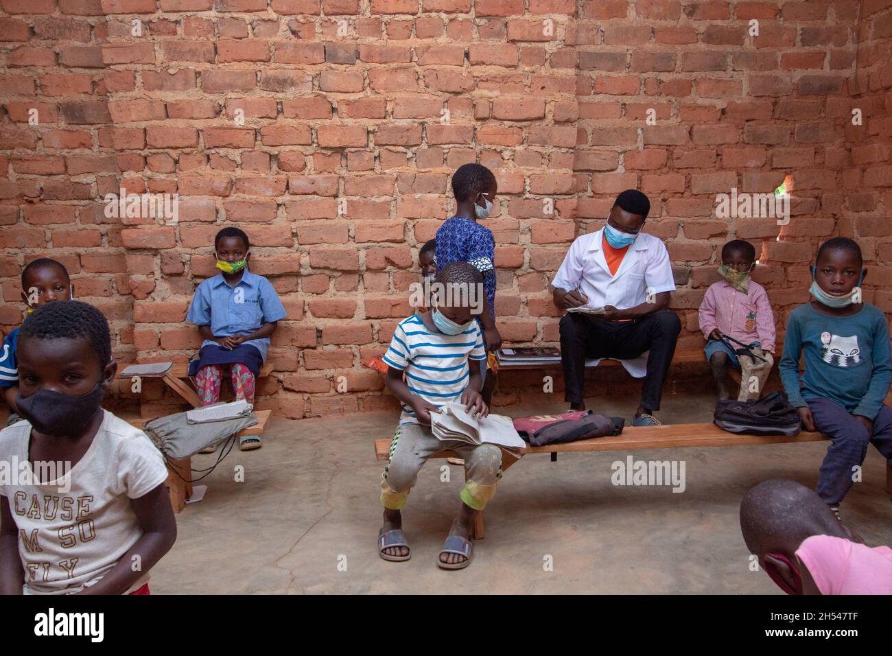 Teacher checking homework in a mud brick classroom, with students ...