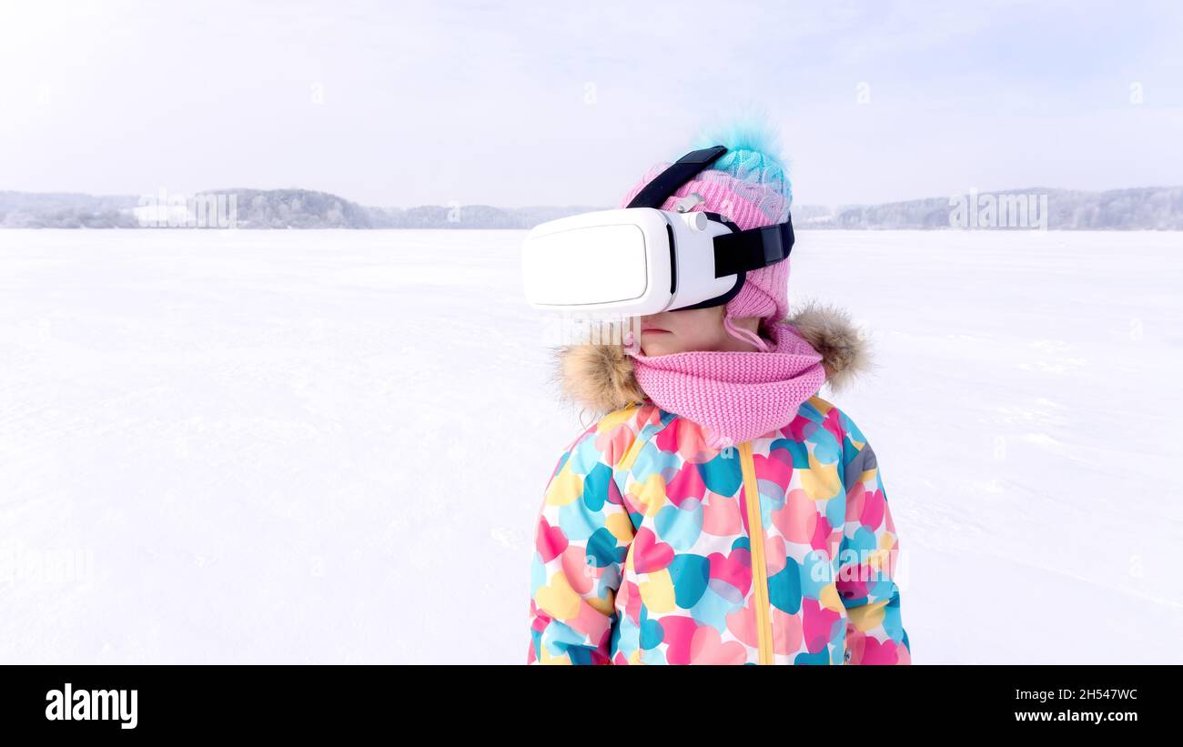 A girl wearing vr glasses stands in the middle of a snow-covered field ...