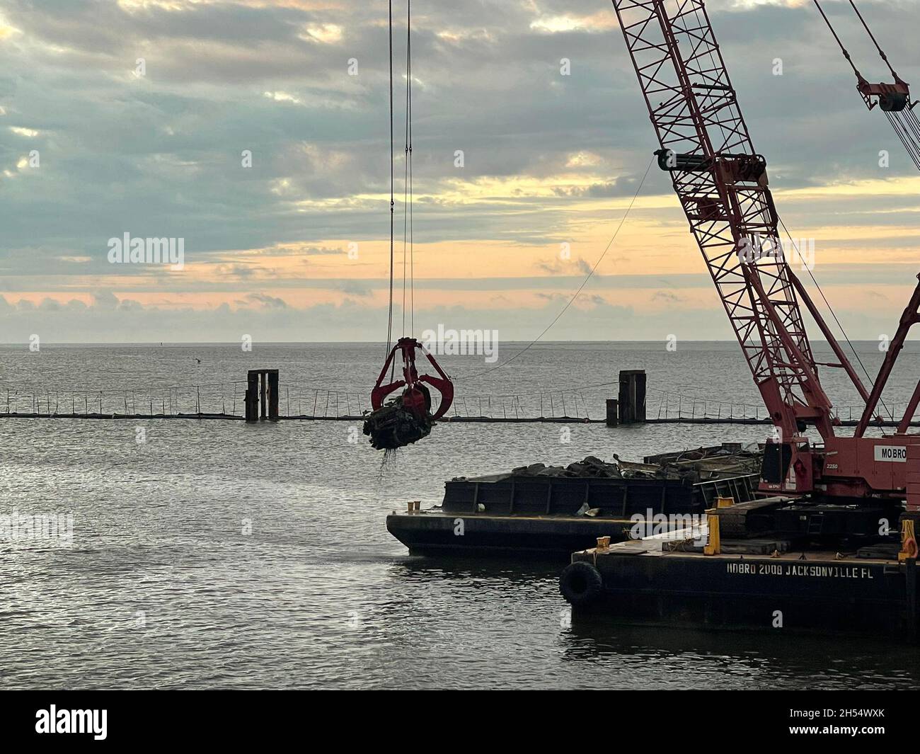 A crane operator lifts a section of a vehicle during debris removal ...
