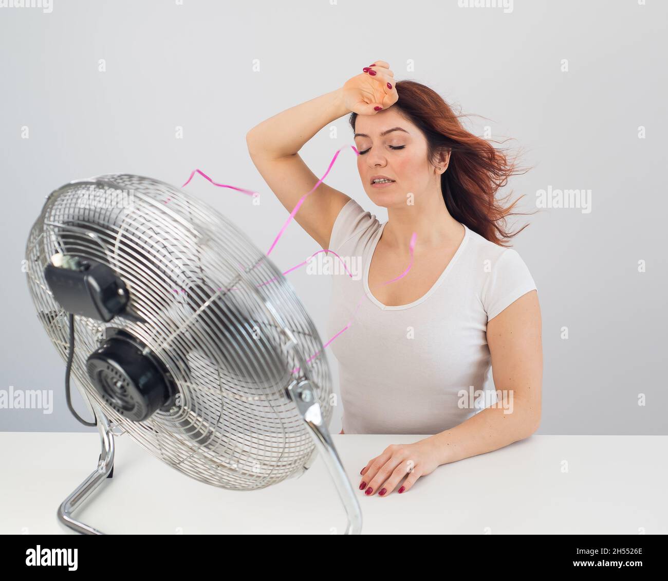 Joyful caucasian woman enjoying the wind blowing from an electric fan ...