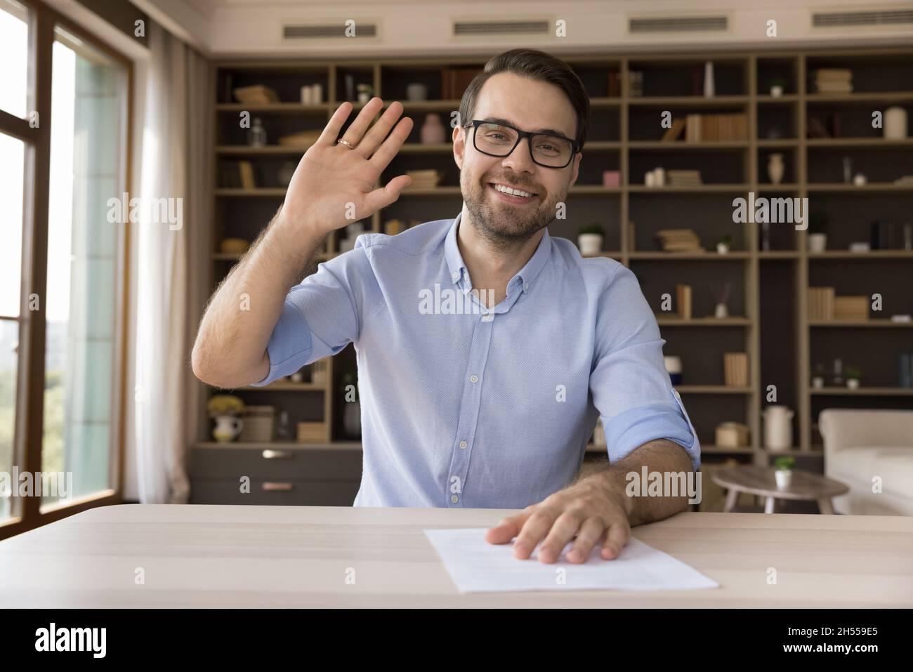 Happy handsome young man waving hand looking at camera Stock Photo - Alamy