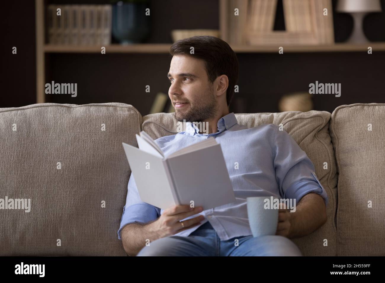 Happy dreamy relaxed young man reading book, drinking coffee Stock ...
