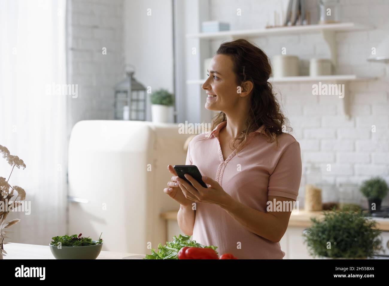 Distracted dreamy young woman using cellphone, cooking in kitchen Stock ...