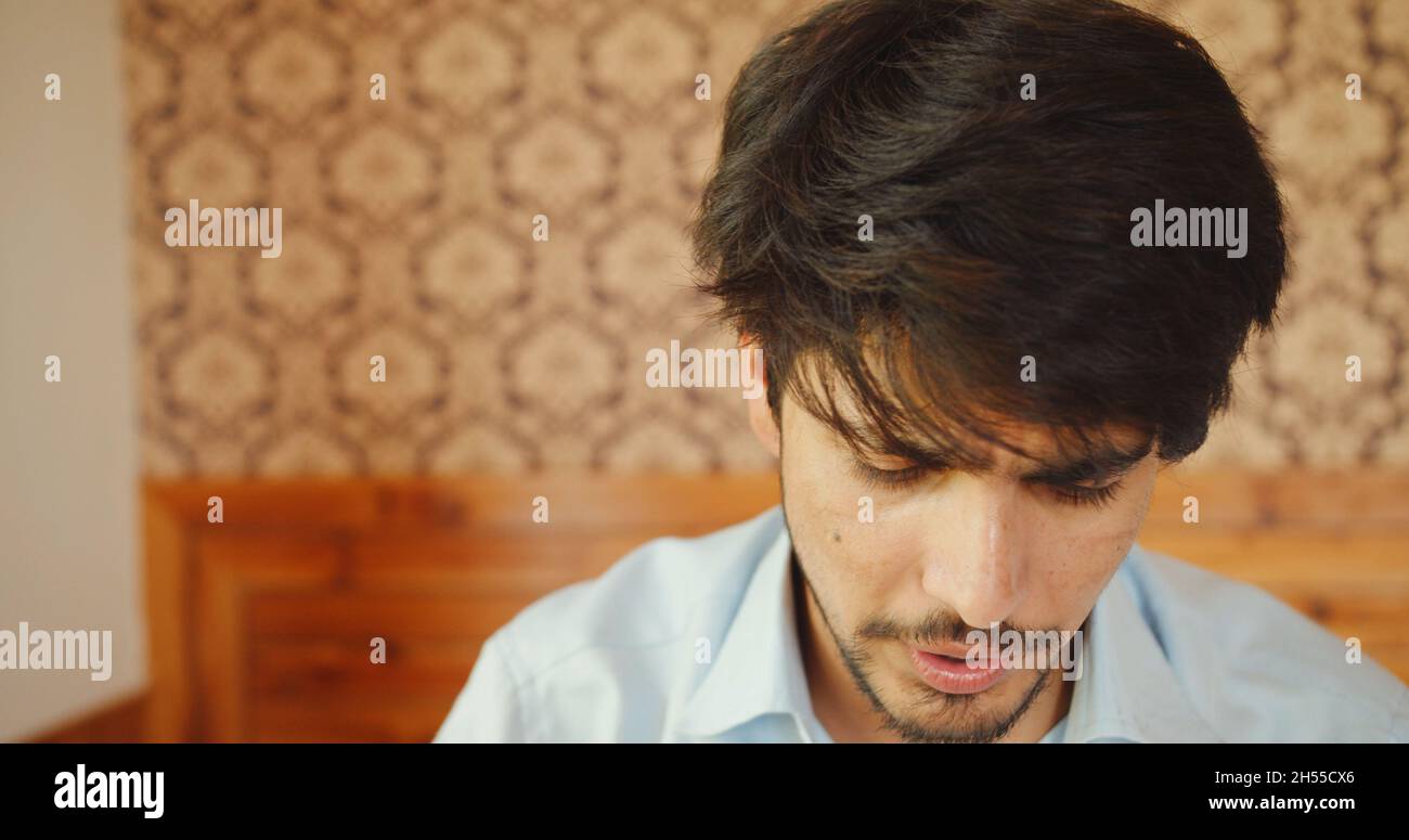 A close up shot of a South Asian man is indoor and looking down on ...