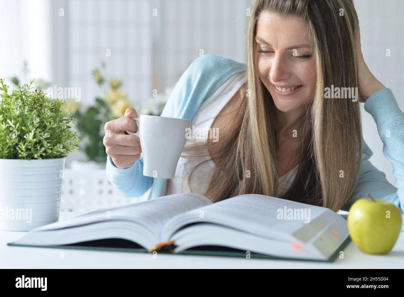 Beautiful young woman with cup of tea and reading book Stock Photo - Alamy