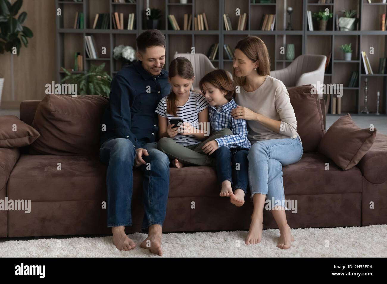 Happy family with kids using smartphone together, sitting on couch ...