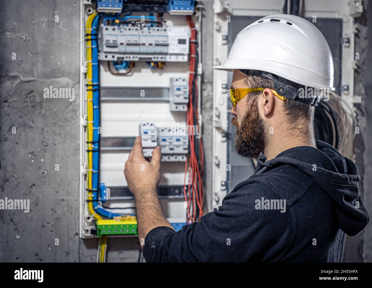 A male electrician works in a switchboard with an electrical connecting ...