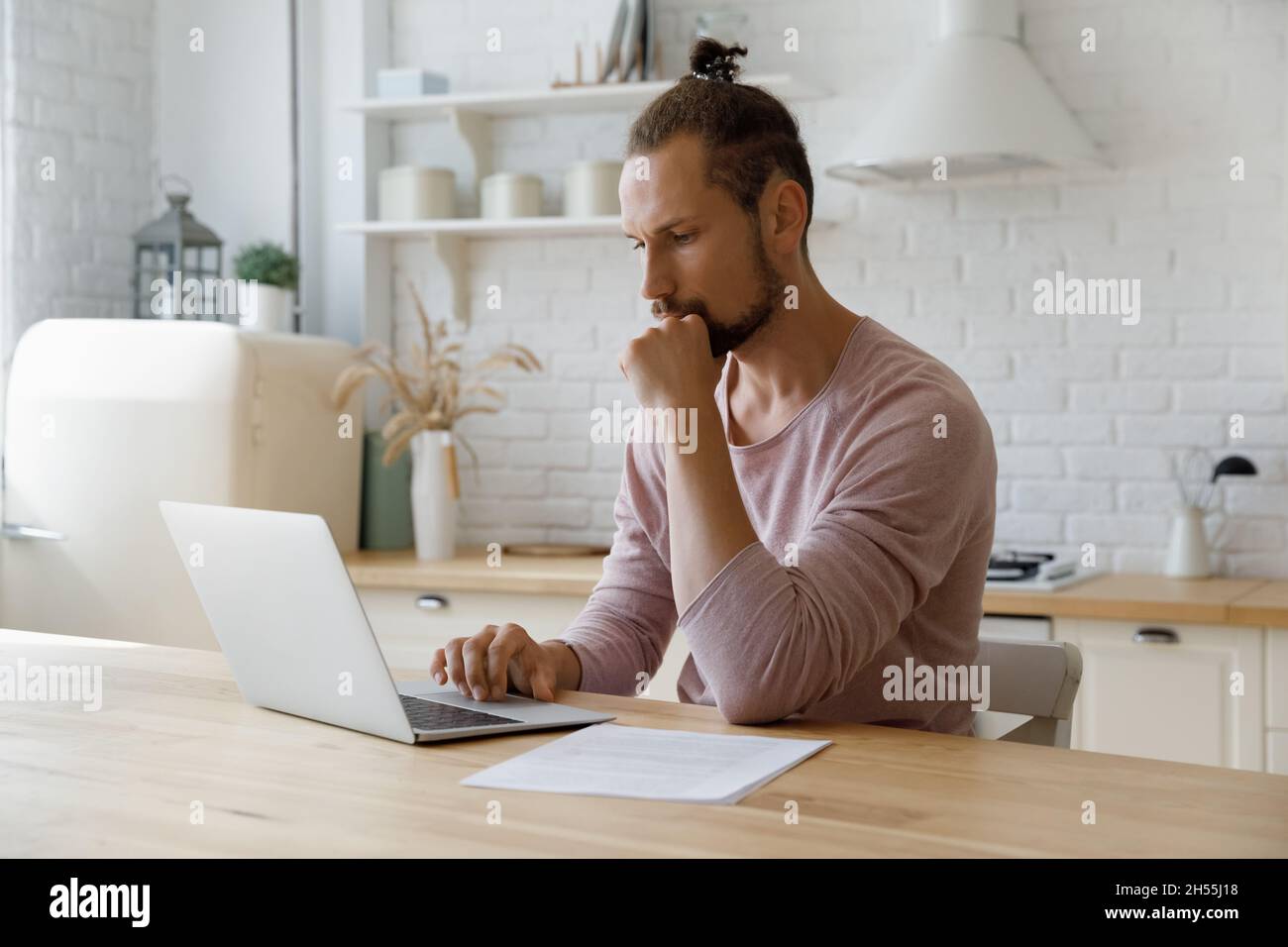 Thoughtful young freelancer working on computer in kitchen Stock Photo ...