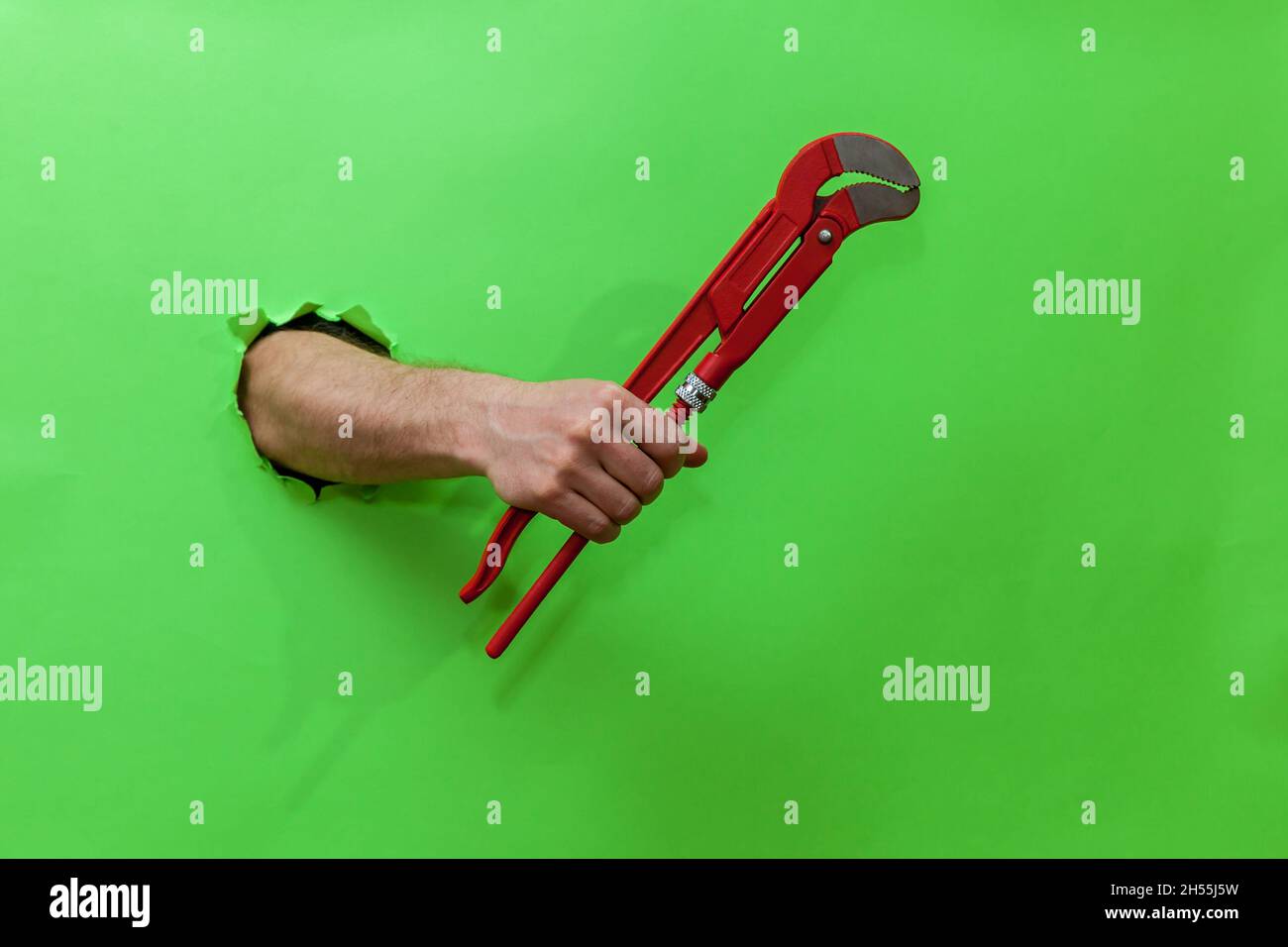 Male hand holds a red pipe key through a torn green paper. Hand through ...