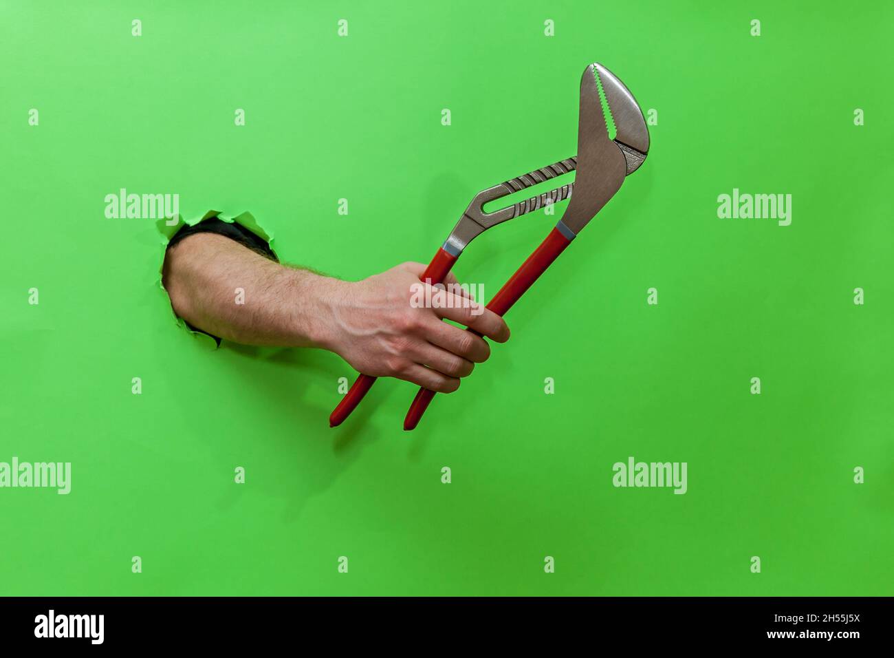 Male hand holds a red pipe key through a torn green paper. Hand through ...