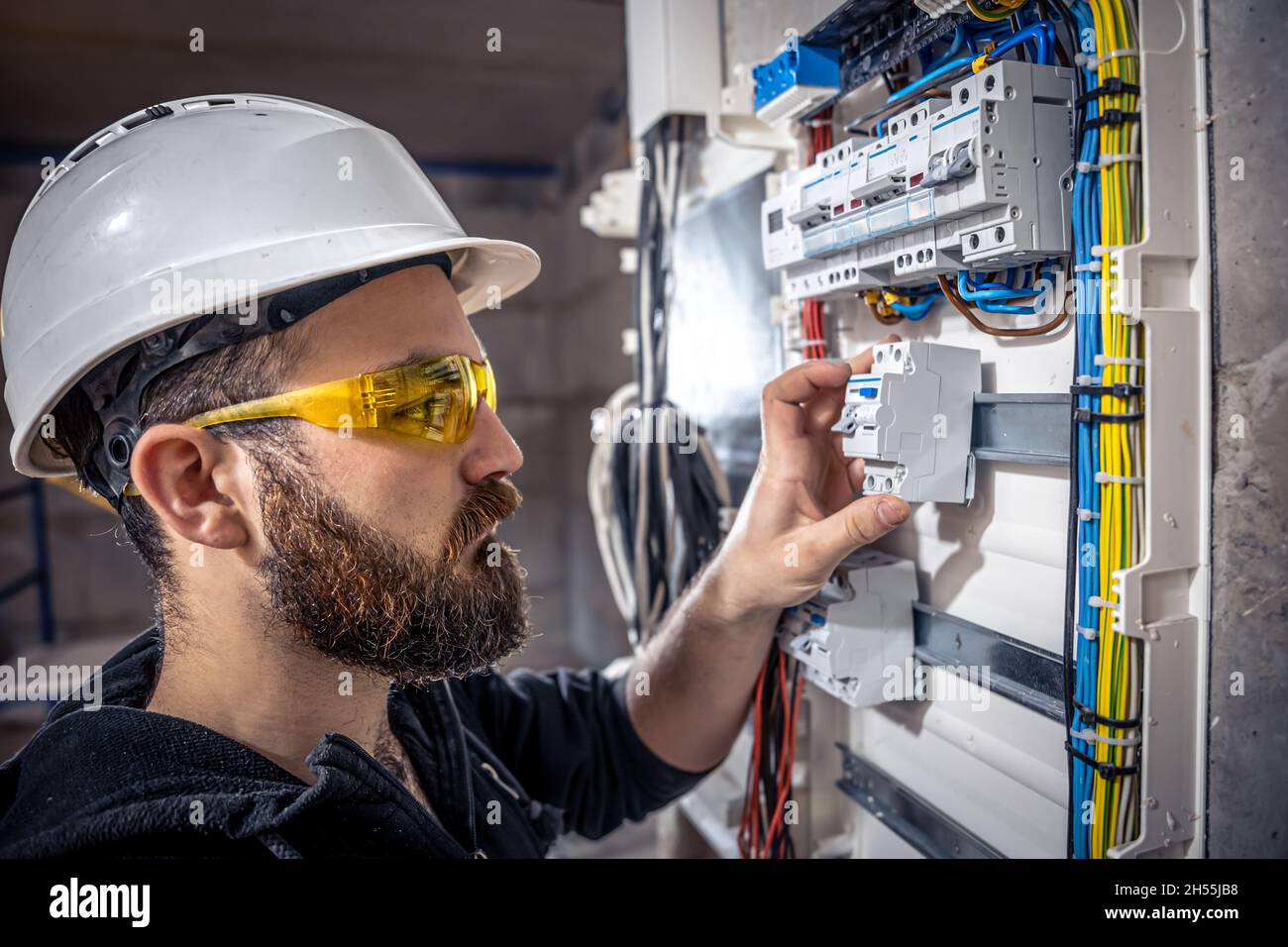 A male electrician works in a switchboard with an electrical connecting ...