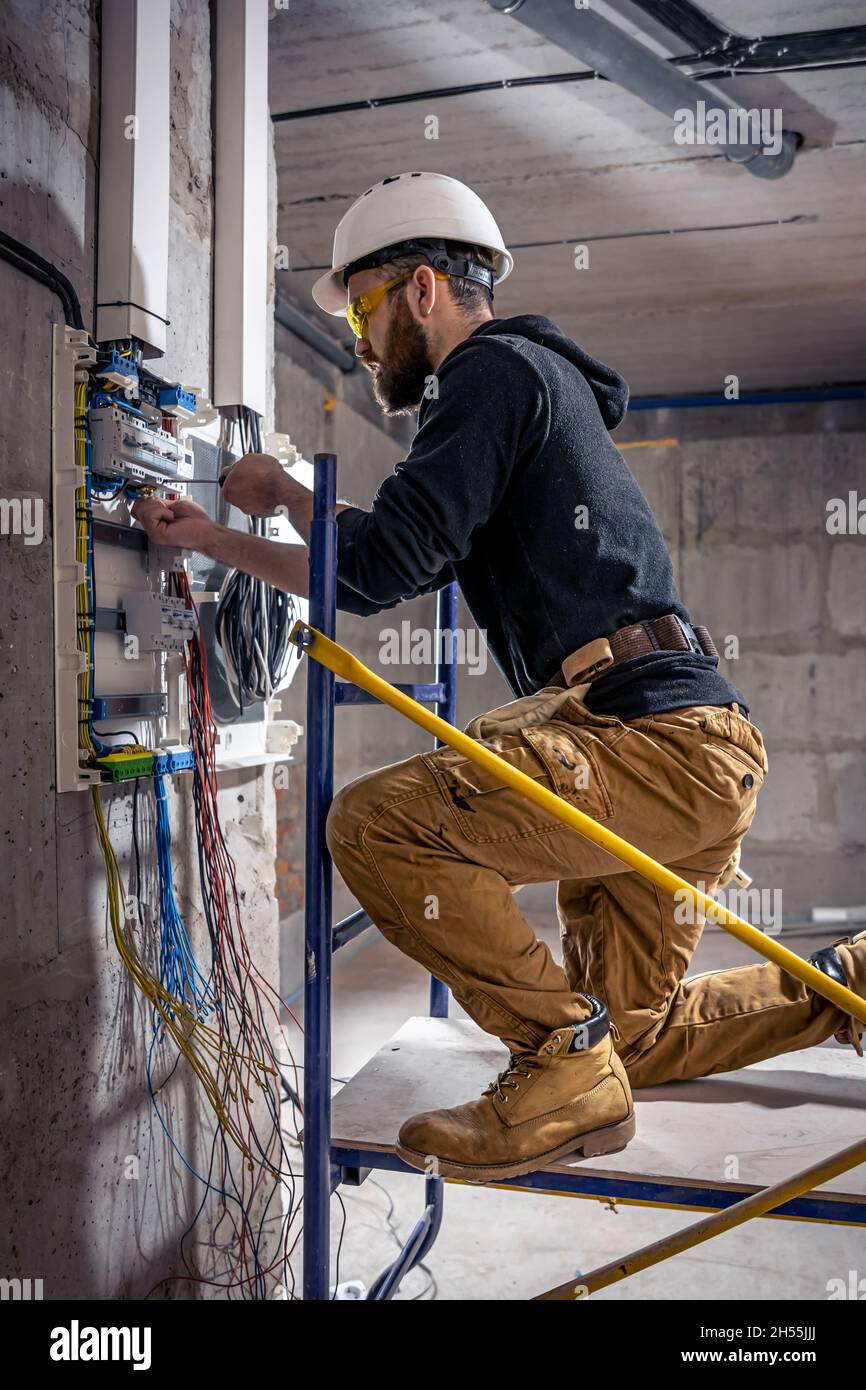A male electrician works in a switchboard with an electrical connecting ...