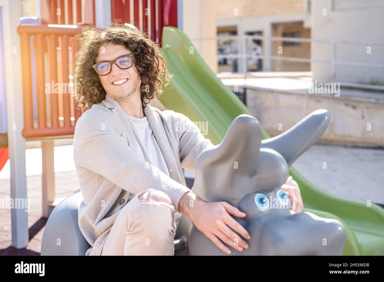 Young man reliving his childhood by playing in a children's playground ...