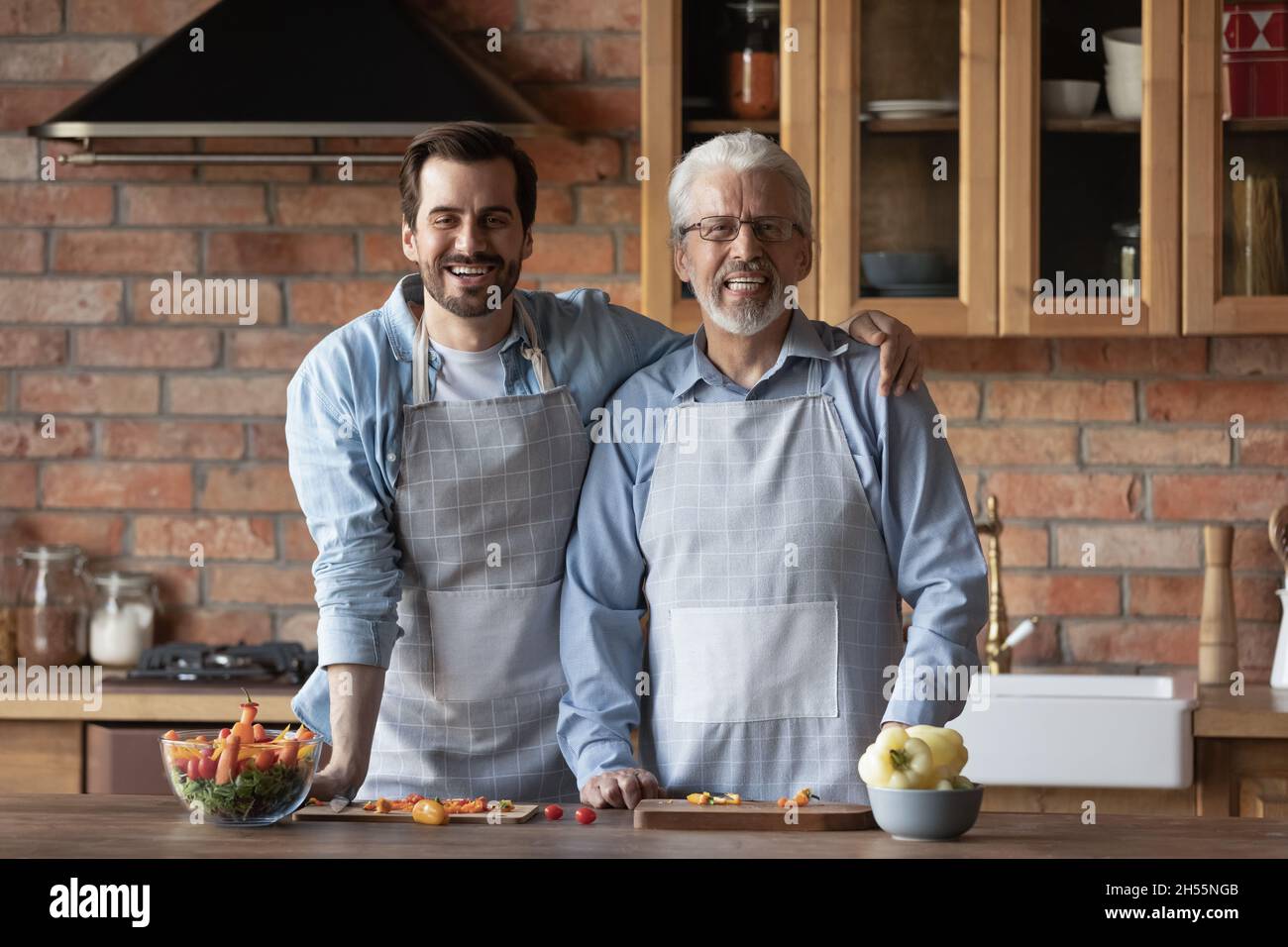Portrait Of Grown Son Hugging Mature Father Cooking At Kitchen Stock