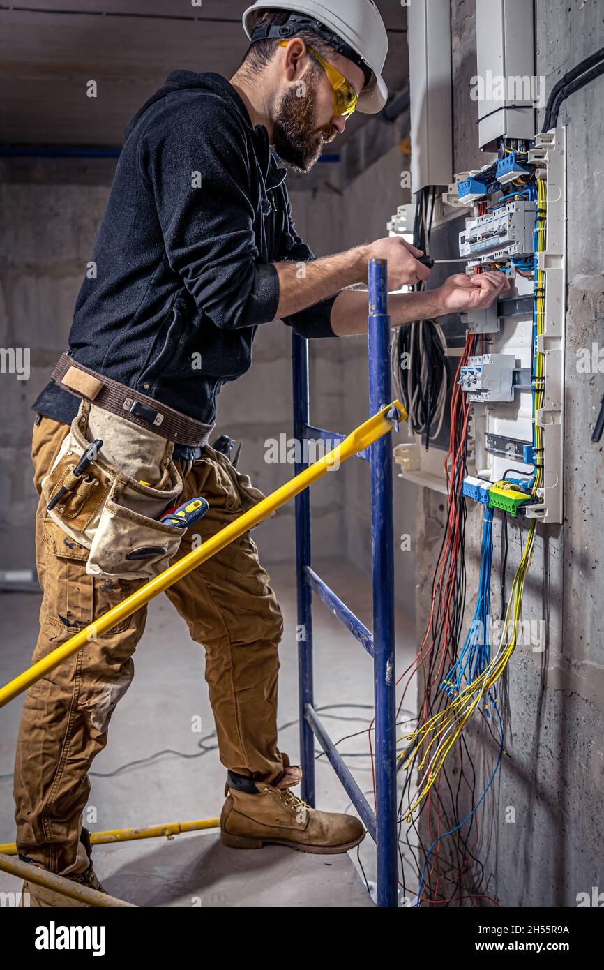 A male electrician works in a switchboard with an electrical connecting ...