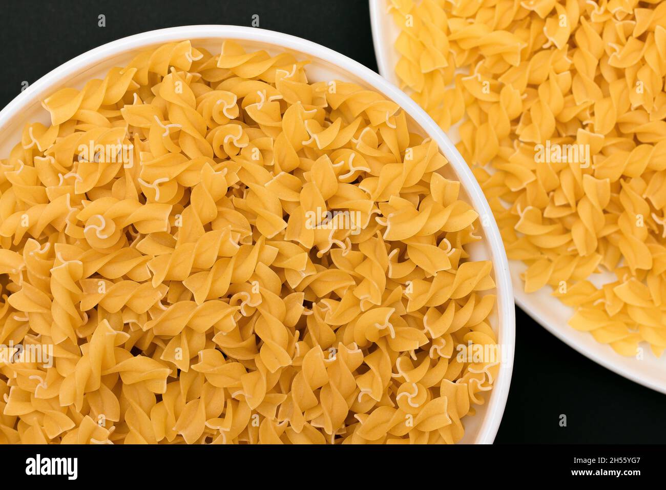 Uncooked Fusilli Pasta Lying on White Plate on Black Background. Raw ...