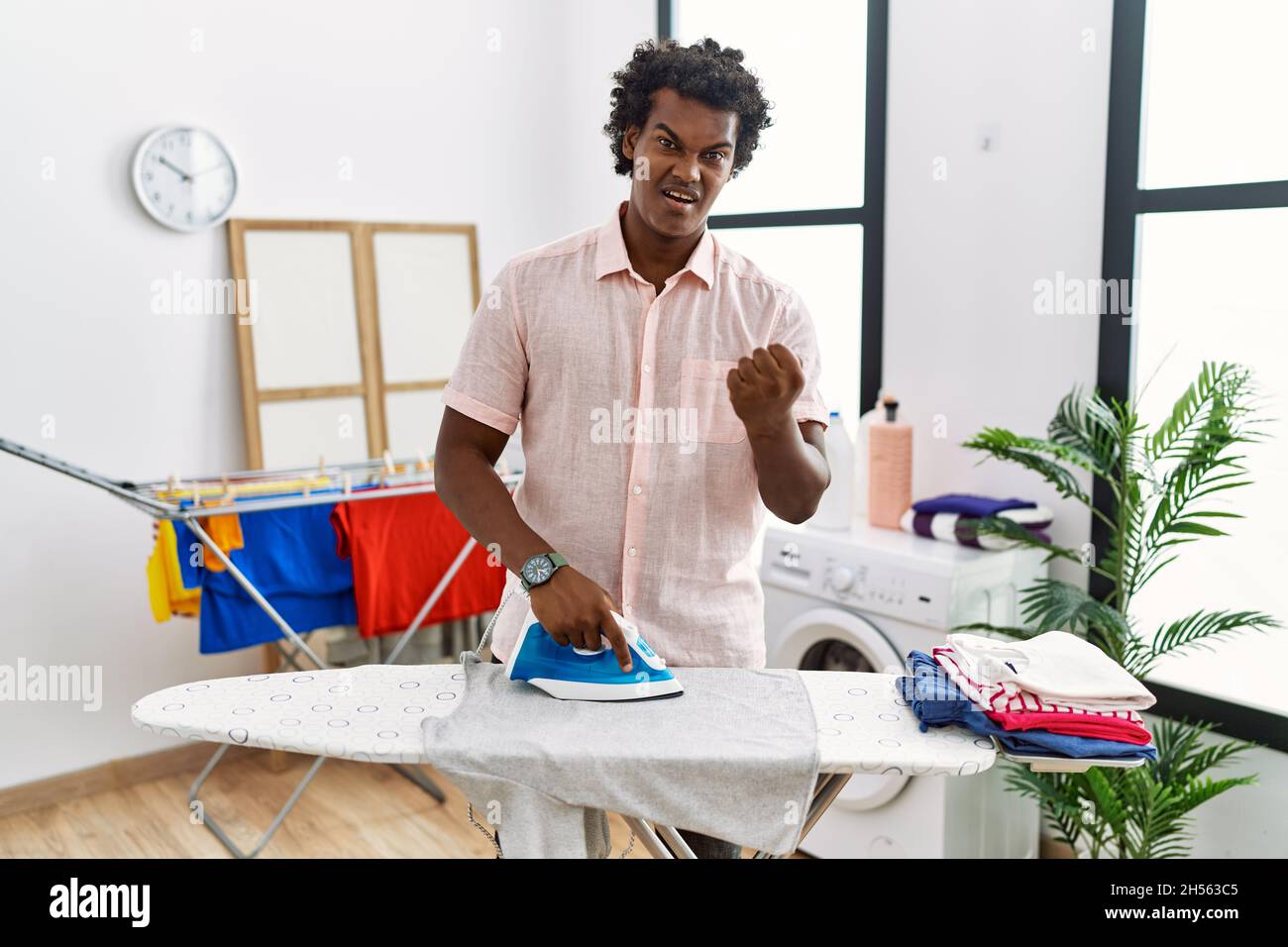 African man with curly hair ironing clothes at home angry and mad ...