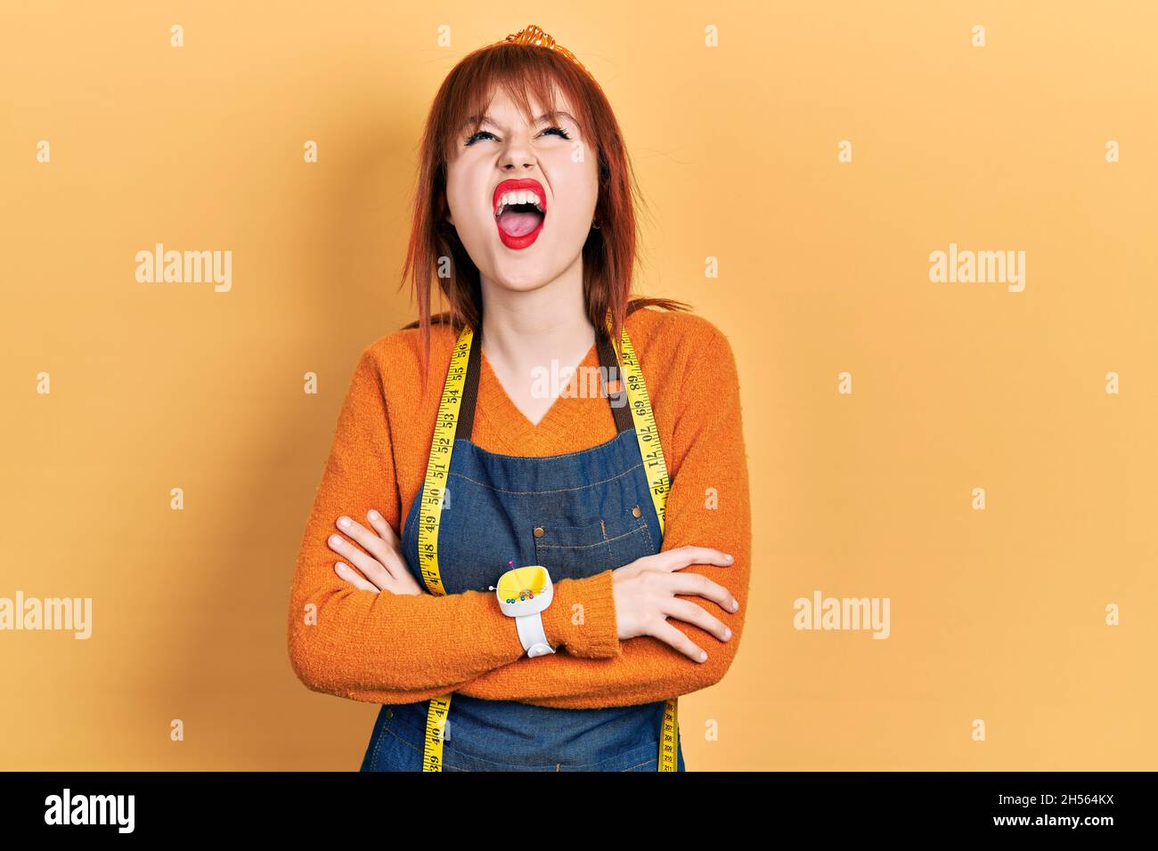 Redhead young woman dressmaker designer wearing atelier apron angry and ...