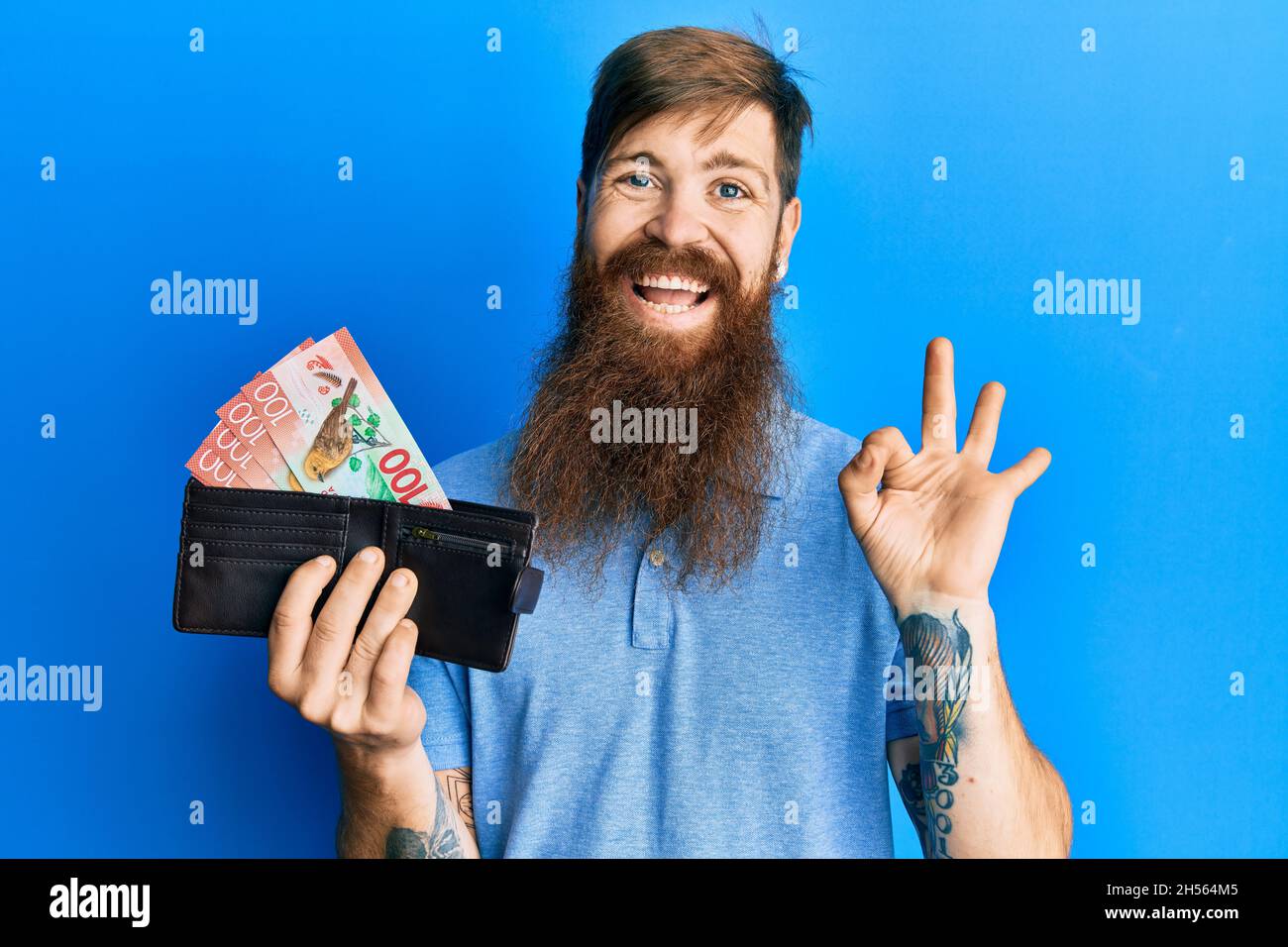Redhead man with long beard holding wallet with new zealand dollars ...