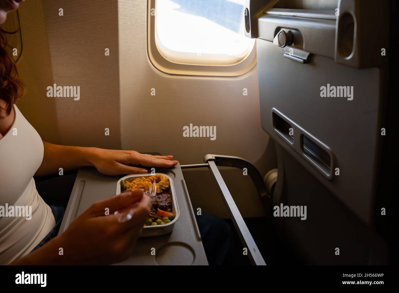 Caucasian woman flying in economy class and eating lunch from a tray ...
