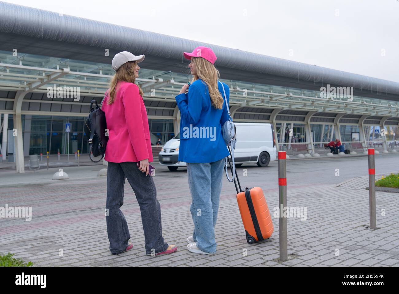 Two happy girls walking near airport, with luggage. Air travel, summer ...
