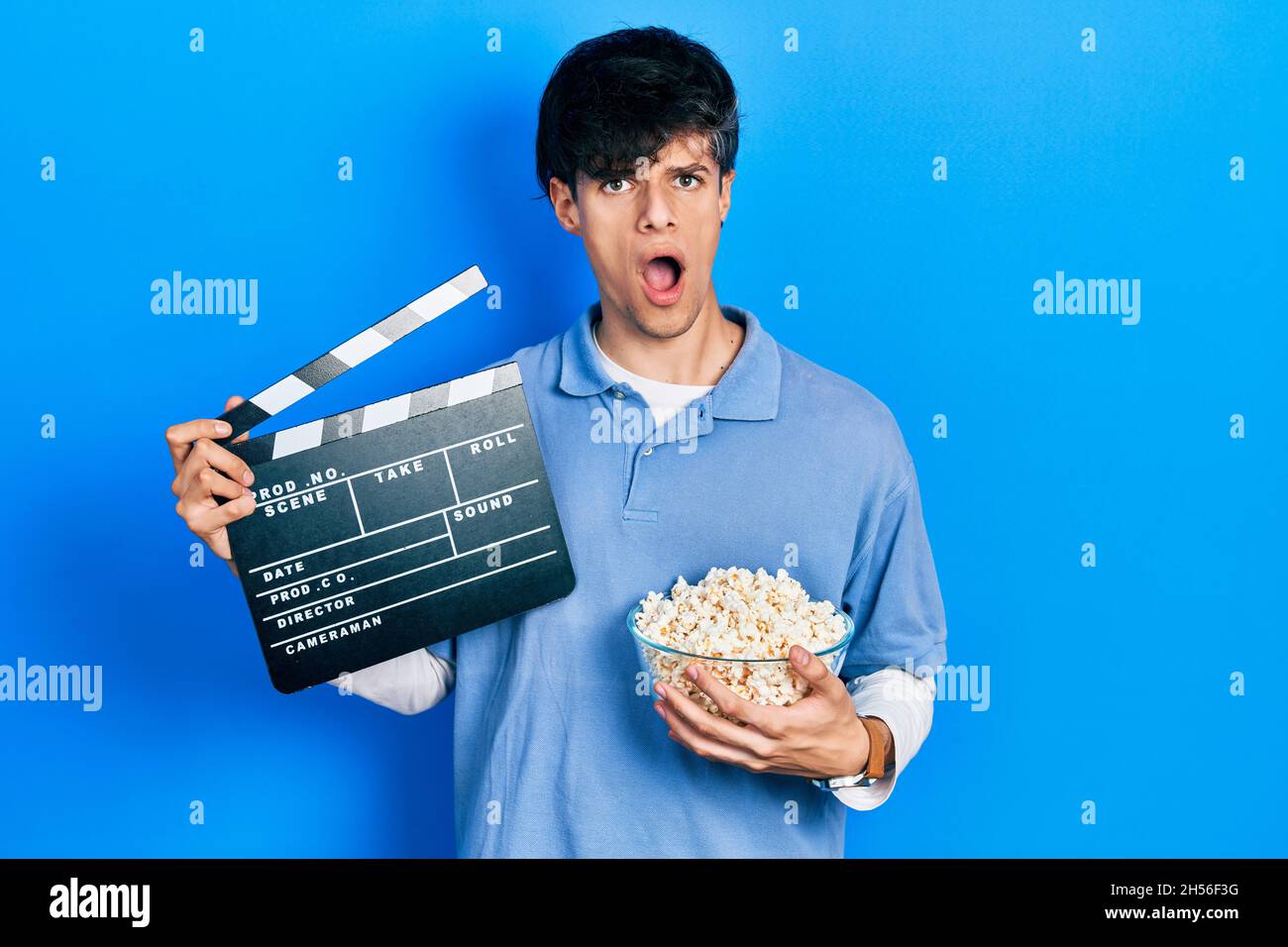 Handsome hipster young man eating popcorn holding cinema clapboard in ...