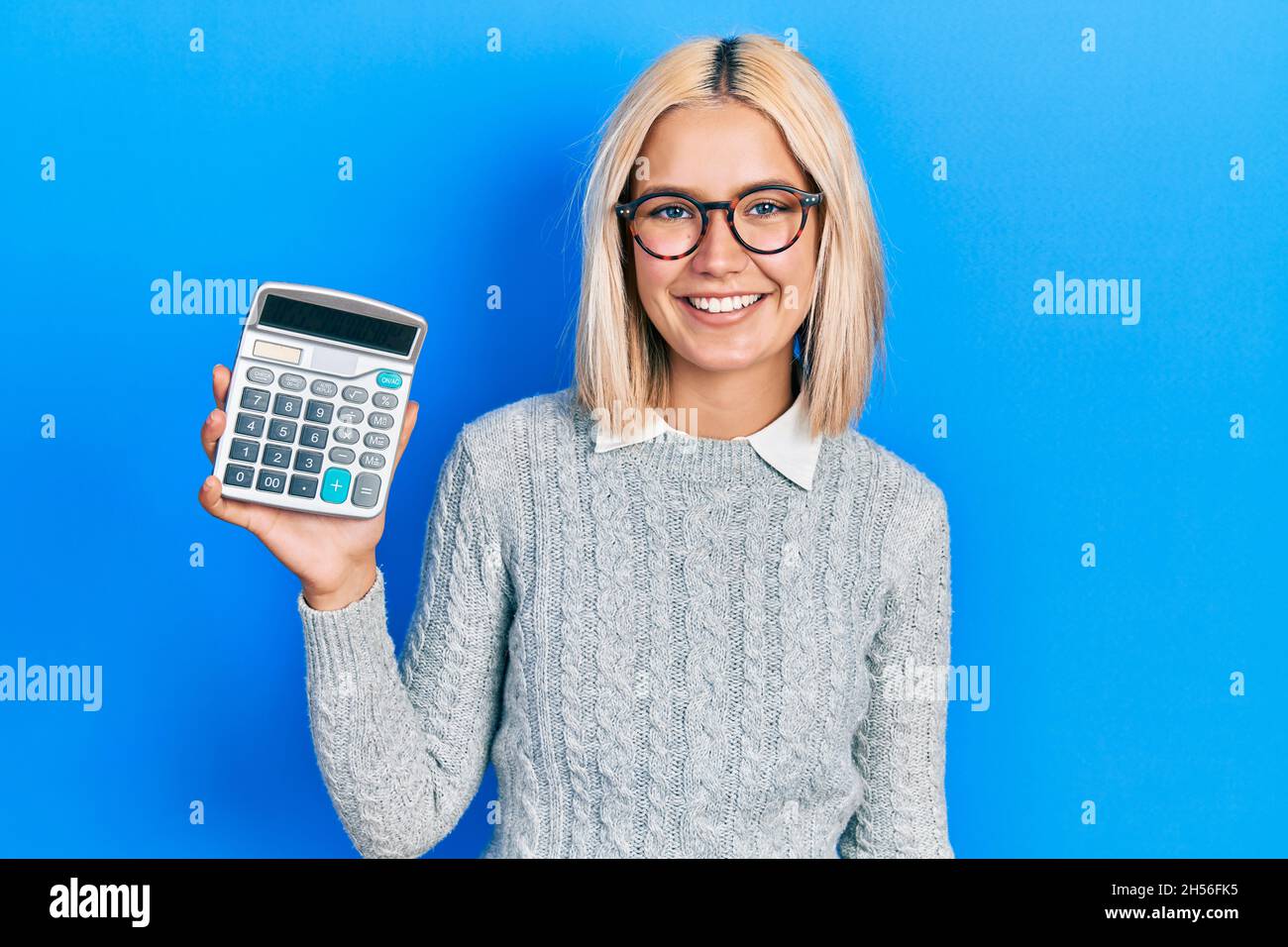Beautiful blonde woman showing calculator device looking positive and ...