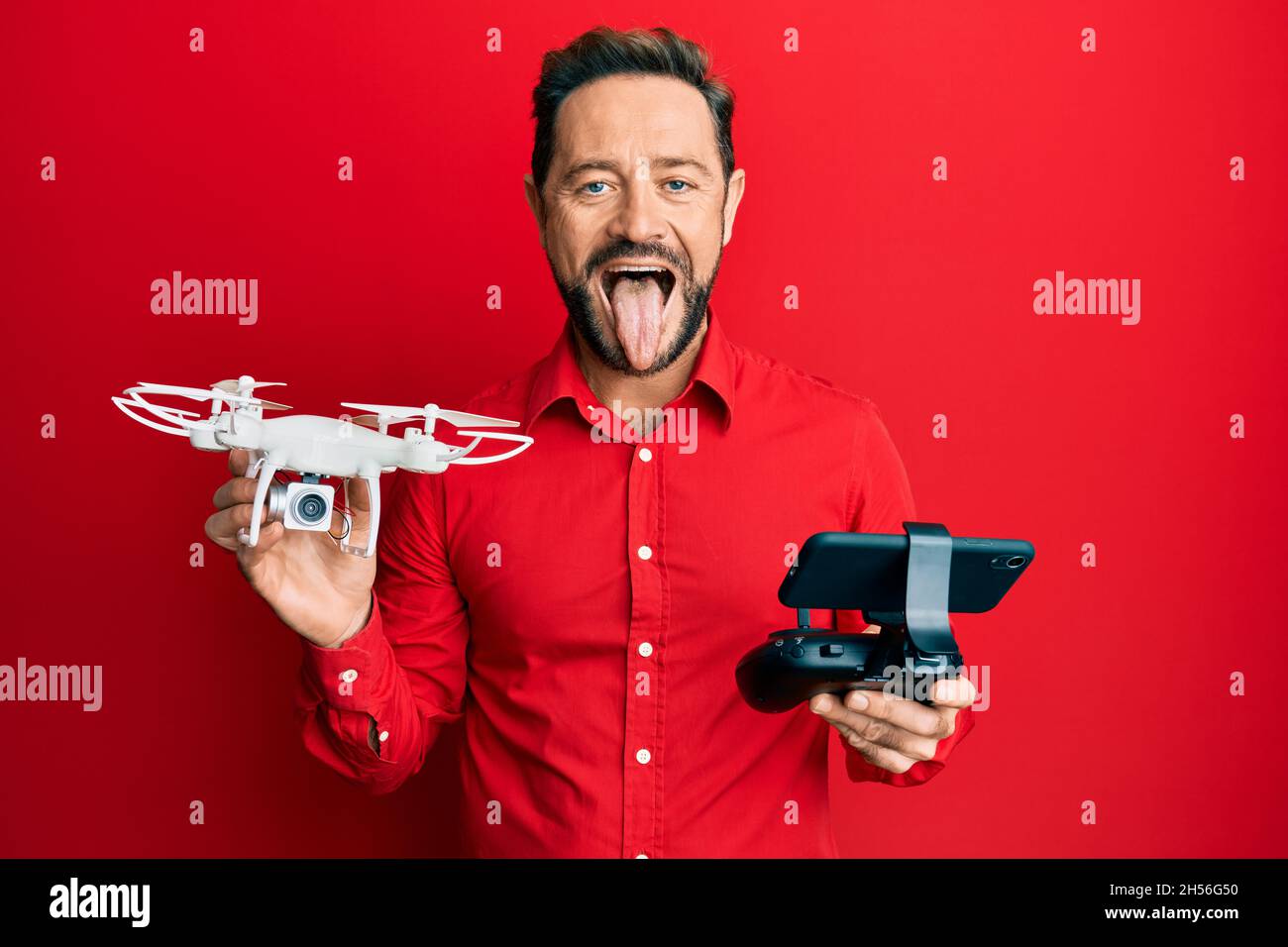 Middle age man using drone sticking tongue out happy with funny ...