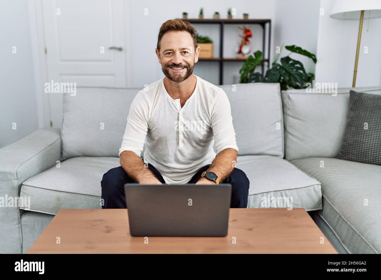 Middle age man using laptop at home with a happy and cool smile on face ...