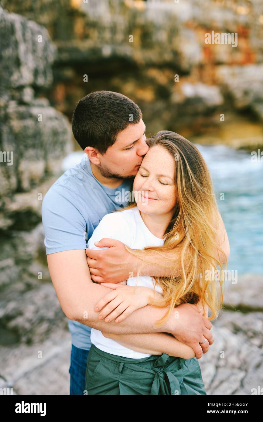Husband hugs from behind and kisses smiling wife against the background ...