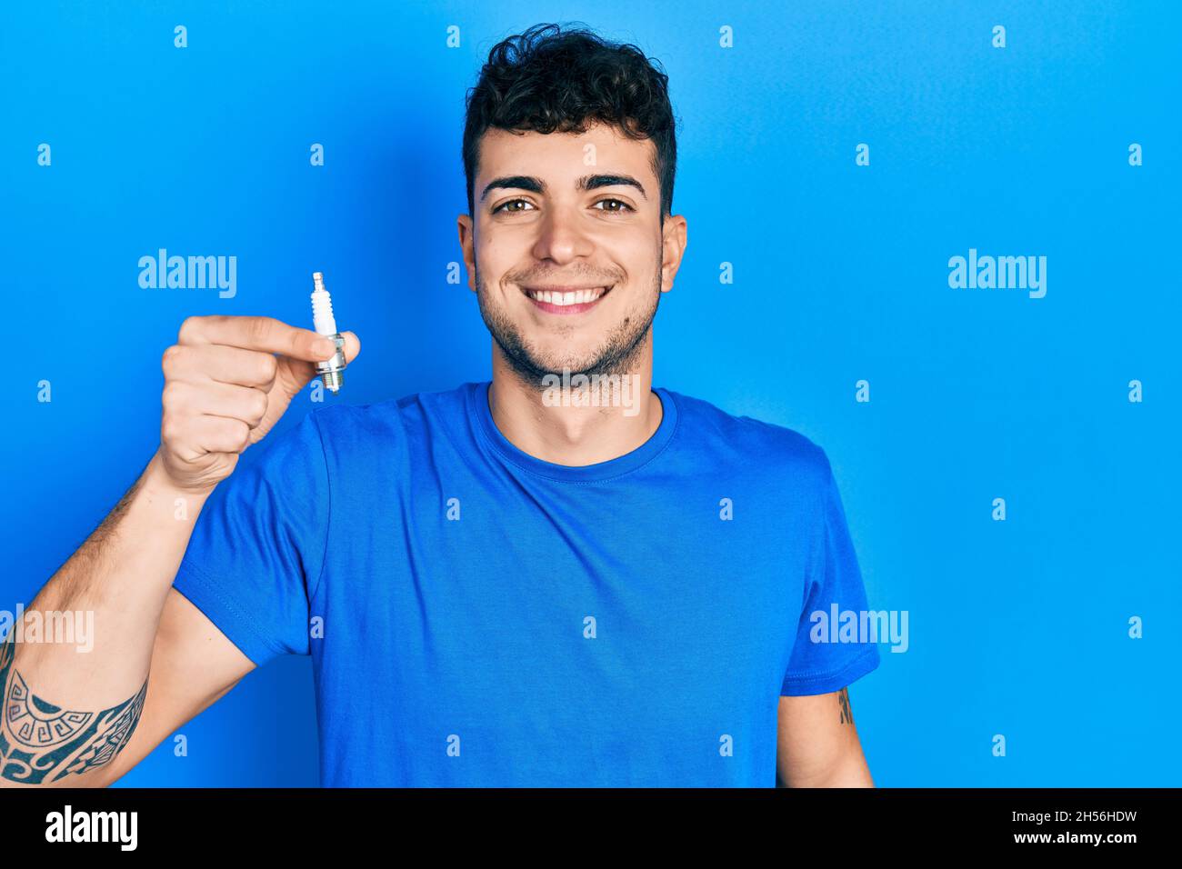 Young hispanic man holding spark plug looking positive and happy ...