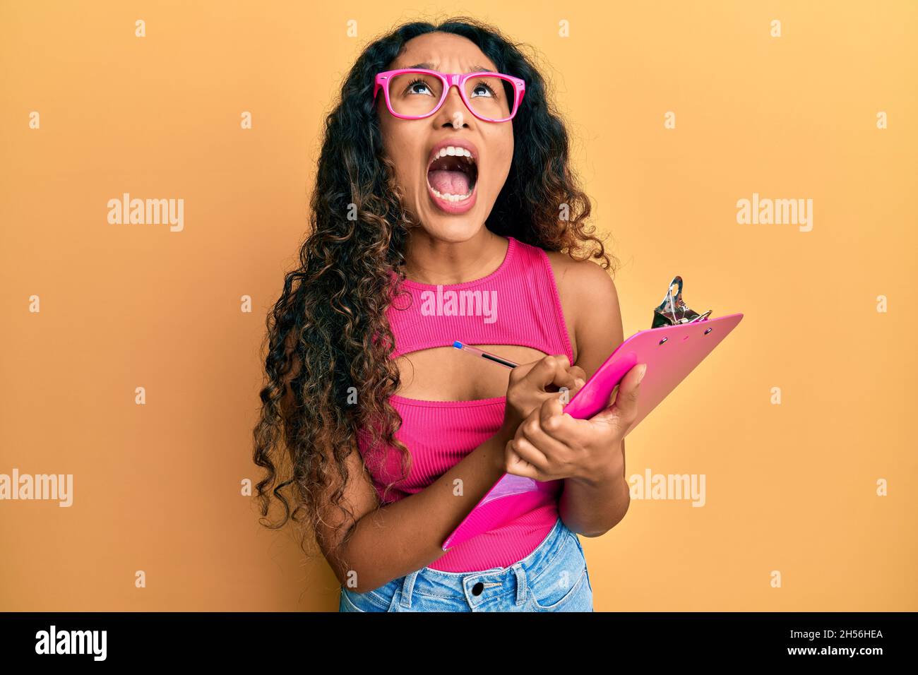 Young latin woman wearing business clothes writing on clipboard angry ...