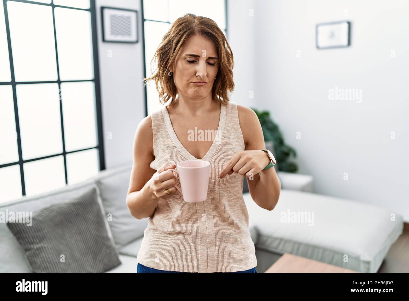 Middle age woman drinking a cup coffee at home pointing down looking ...