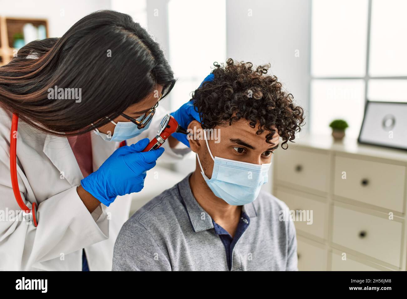 Young latin doctor woman auscultating the ear of man using otoscope at ...