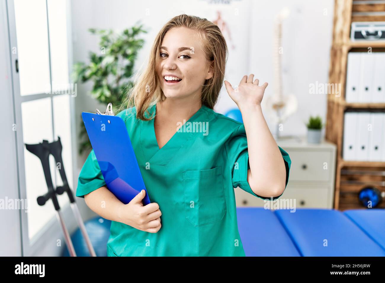 Young caucasian woman working at pain recovery clinic waiving saying ...