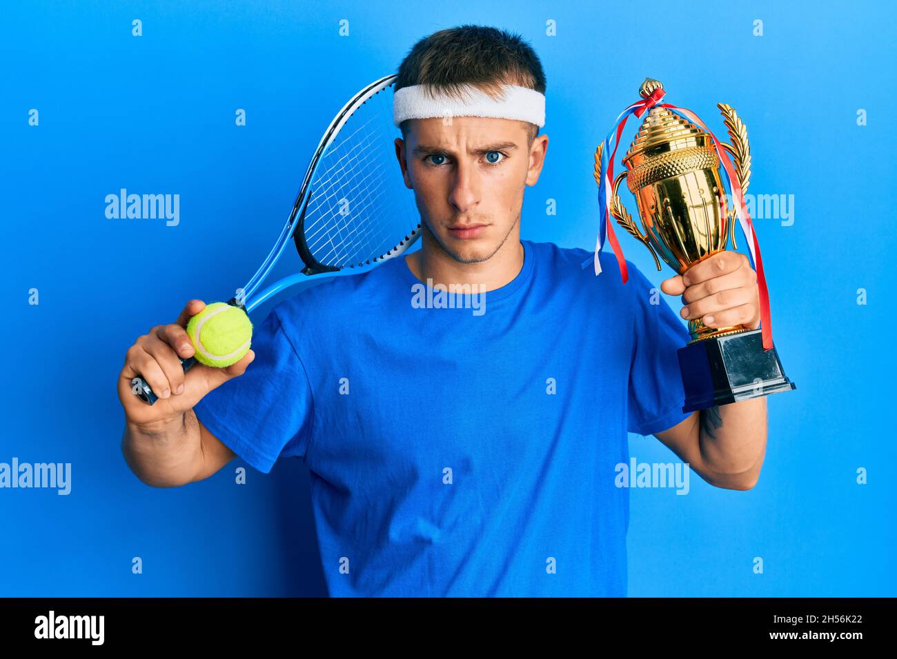 Young caucasian man playing tennis holding trophy skeptic and nervous ...