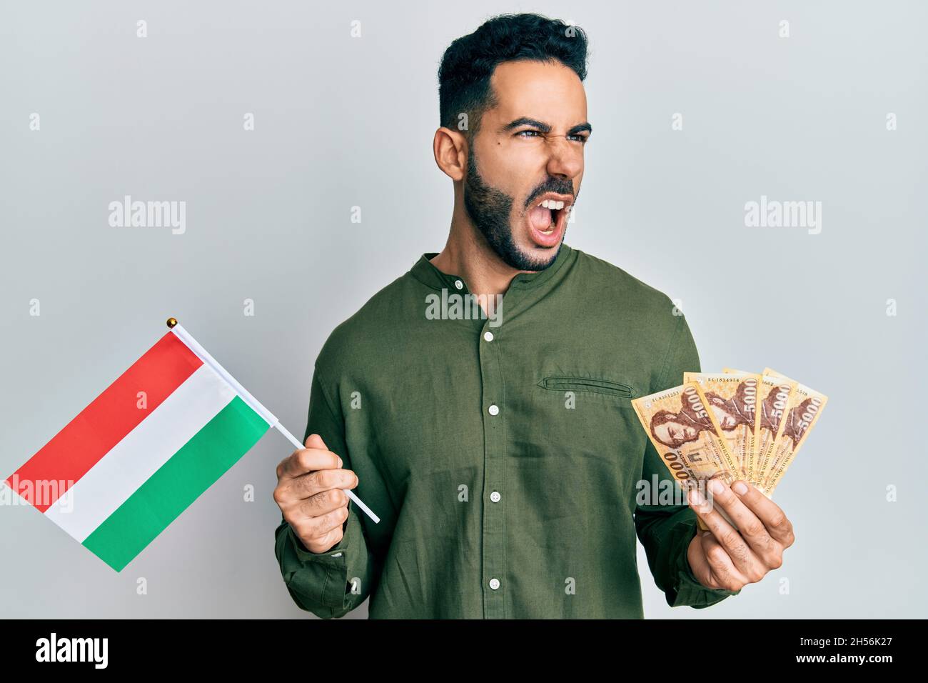 Young hispanic man holding hungary flag and forints angry and mad ...