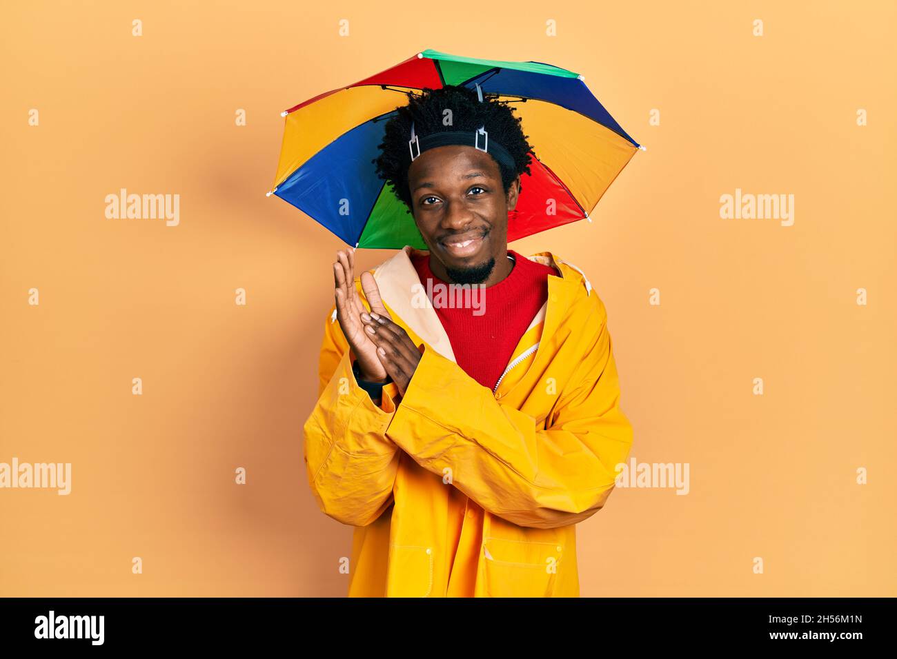 Young african american man wearing yellow raincoat clapping and ...