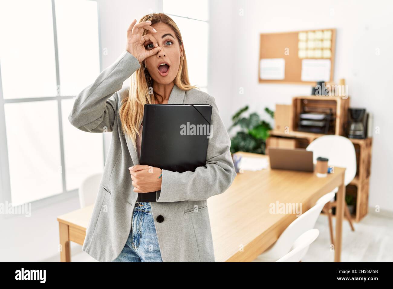 Blonde business woman at the office doing ok gesture shocked with ...