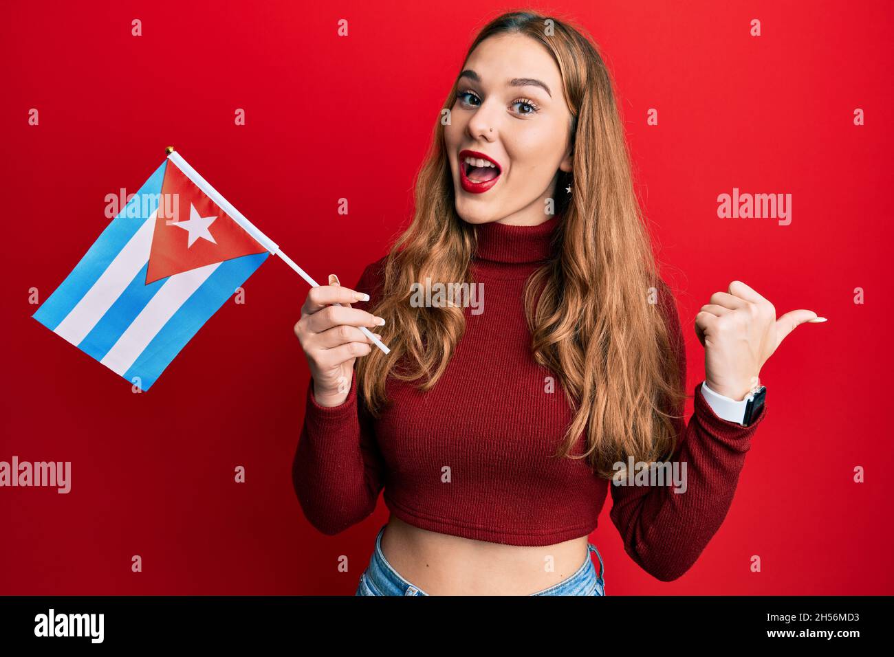 Young blonde woman holding cuba flag pointing thumb up to the side ...