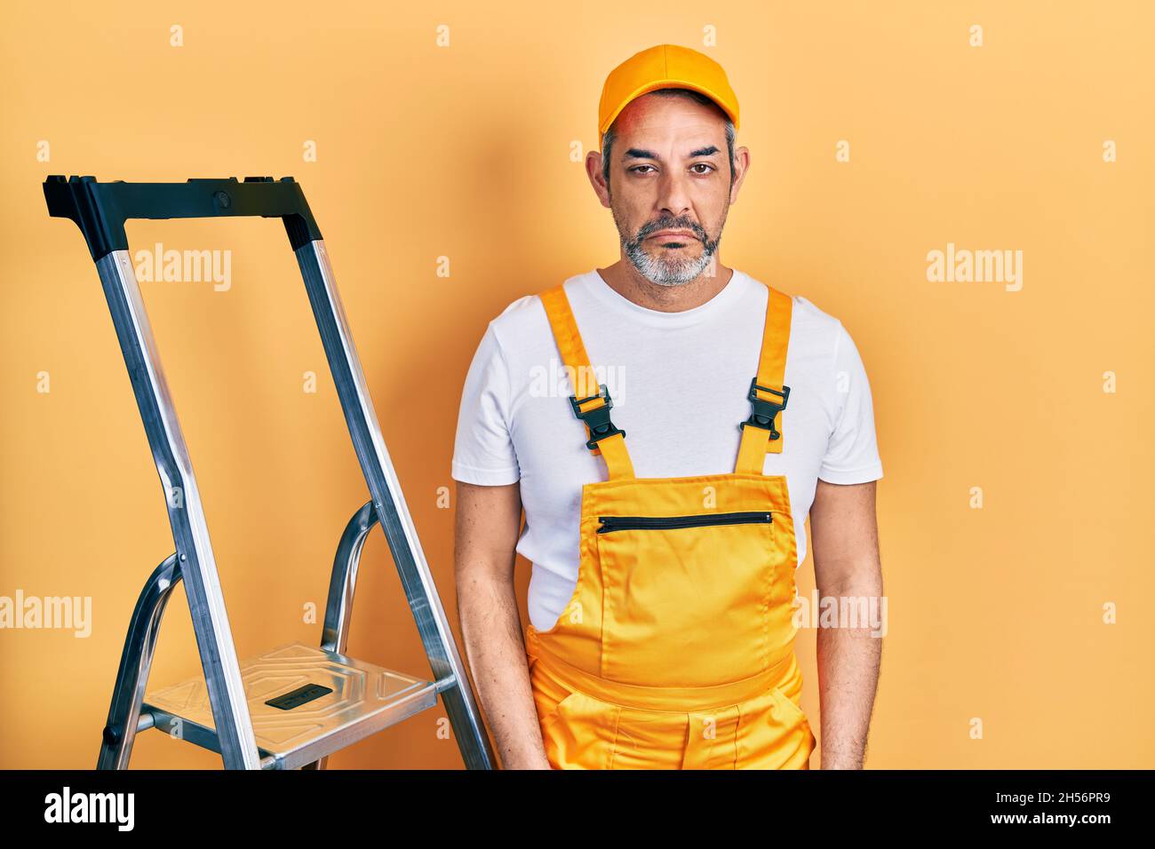 Handsome middle age man with grey hair holding ladder depressed and ...