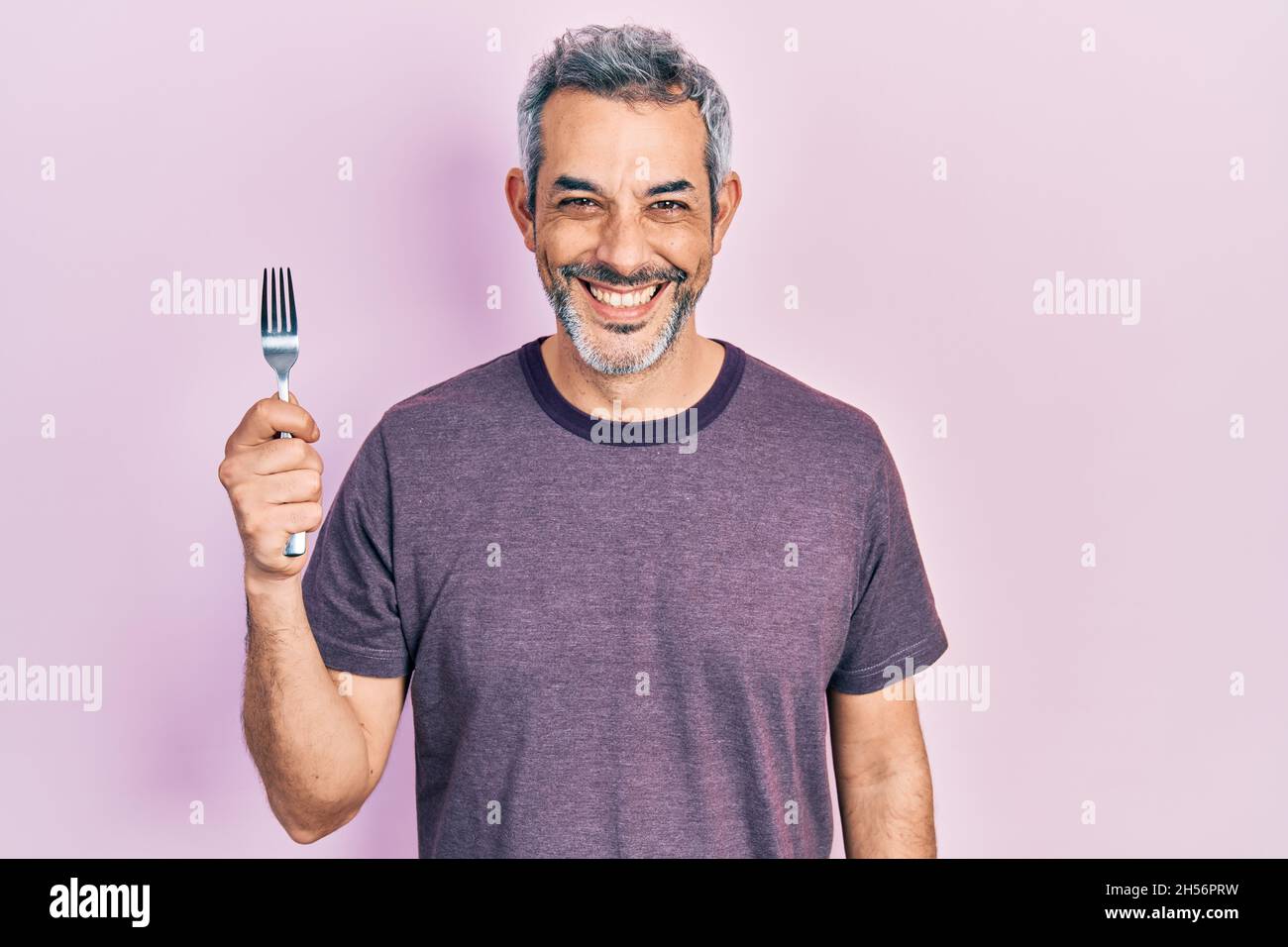 Handsome middle age man with grey hair holding one silver fork looking ...