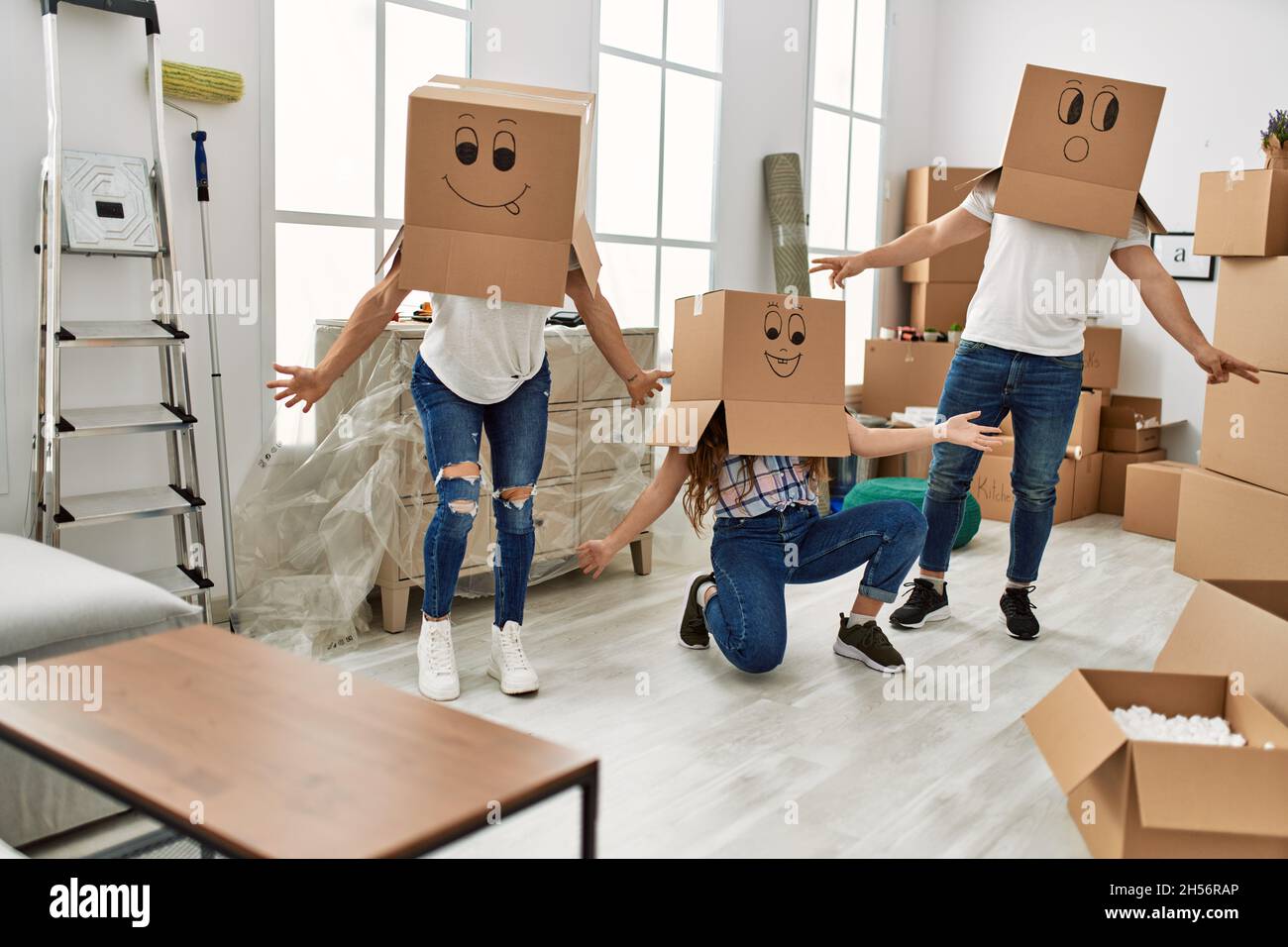 Mother and couple playing with funny cardboard box on head at home ...