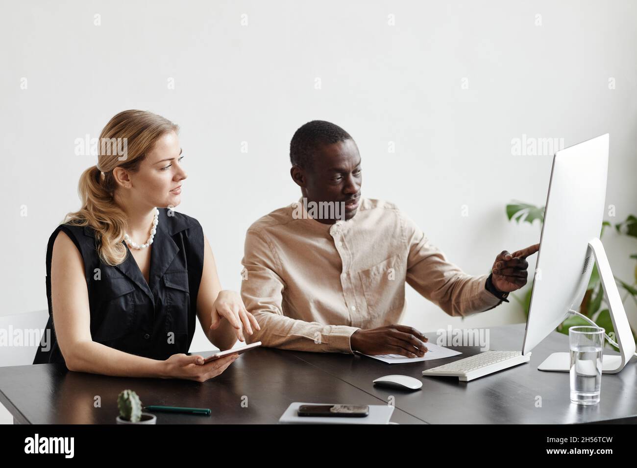 Portrait of two business people looking at computer and pointing at ...