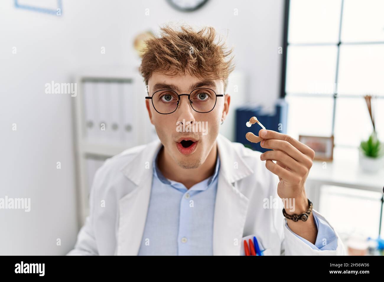 Young caucasian doctor man holding earing aid at the clinic scared and ...