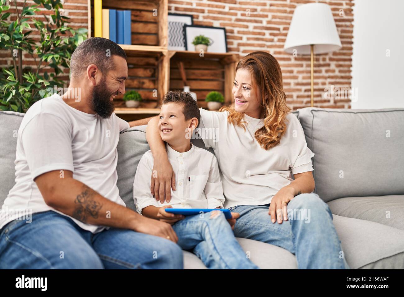 Family using touchpad hugging each other sitting on sofa at home Stock ...