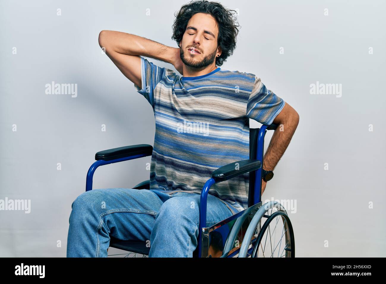Handsome hispanic man sitting on wheelchair suffering of neck ache ...
