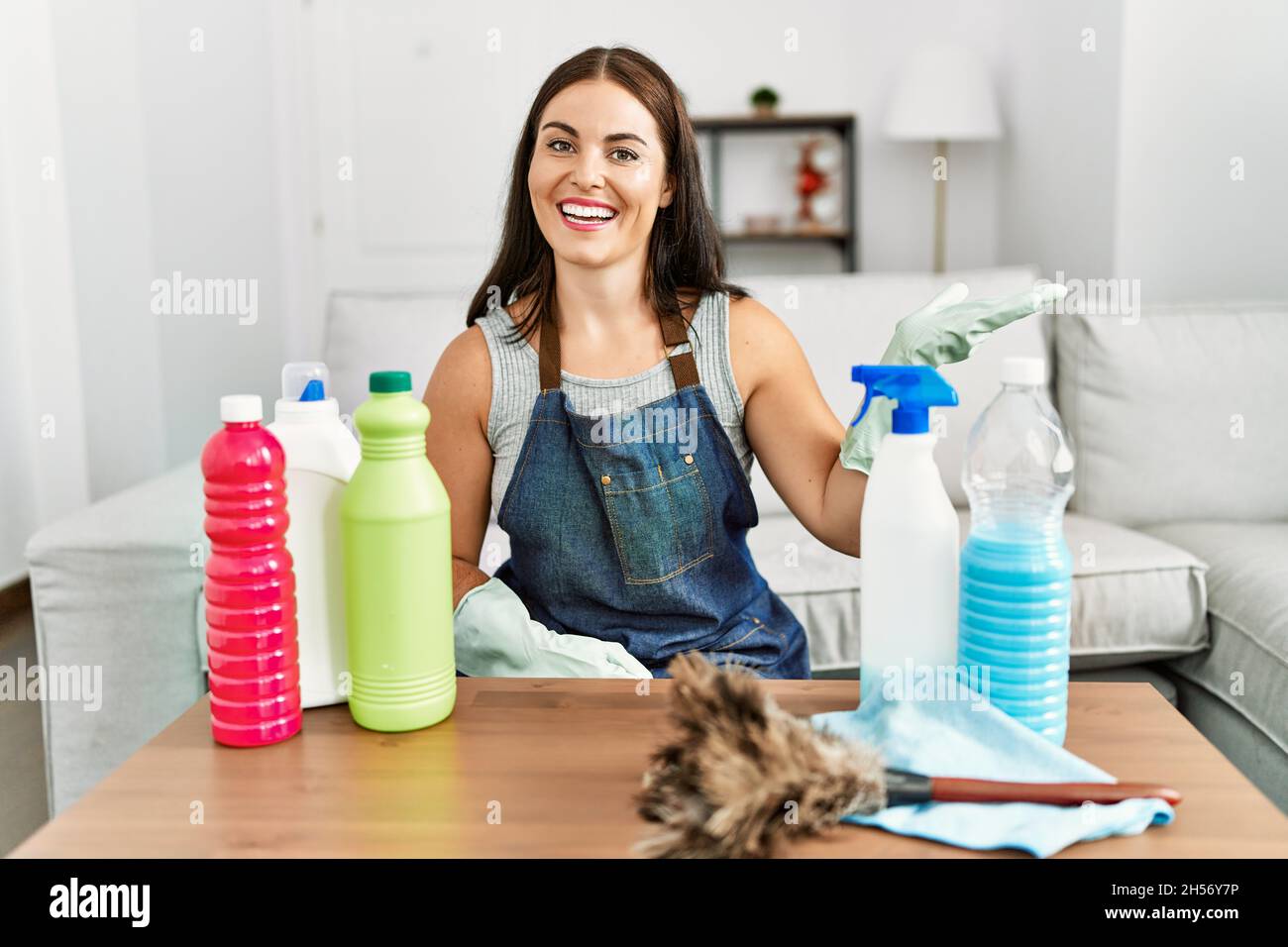 Young brunette woman wearing cleaner apron and gloves cleaning at home ...