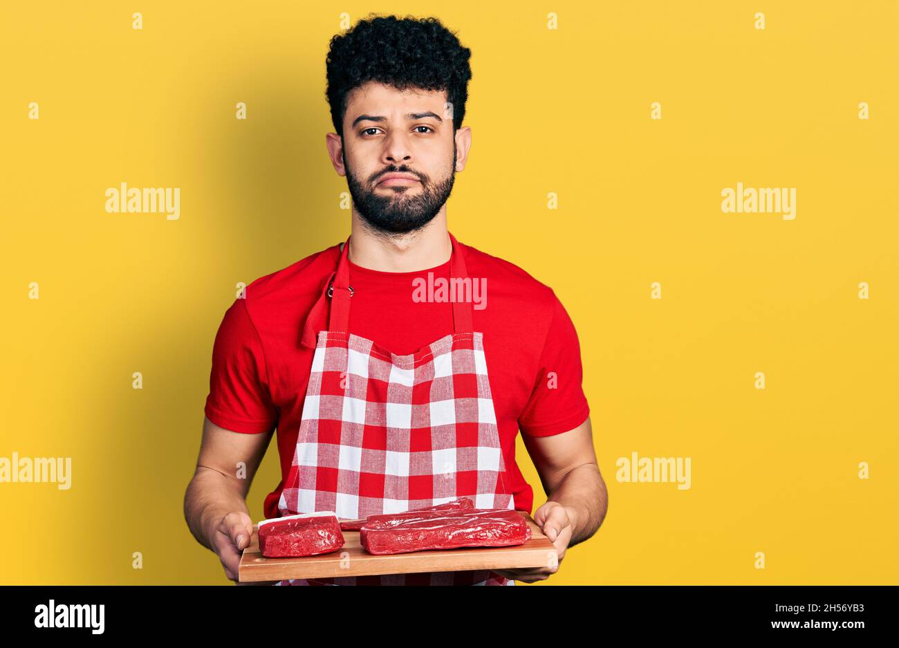 Young arab man with beard holding board with raw meat depressed and ...