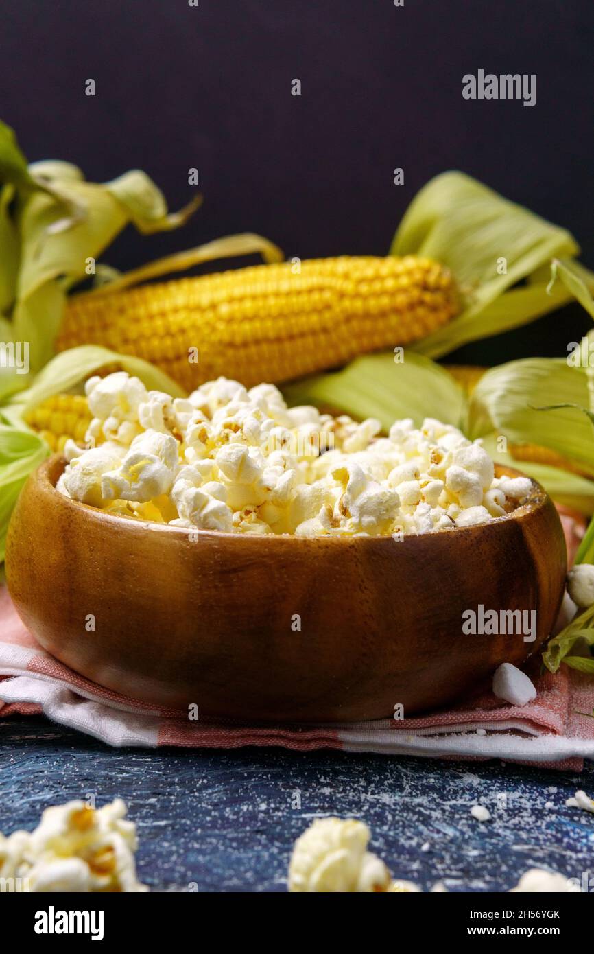 A bowl of popcorn with cobs of fresh corn on a dark background. Leisure ...